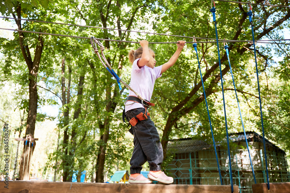 Portrait of brave little girl walk on a rope bridge in an adventure ...