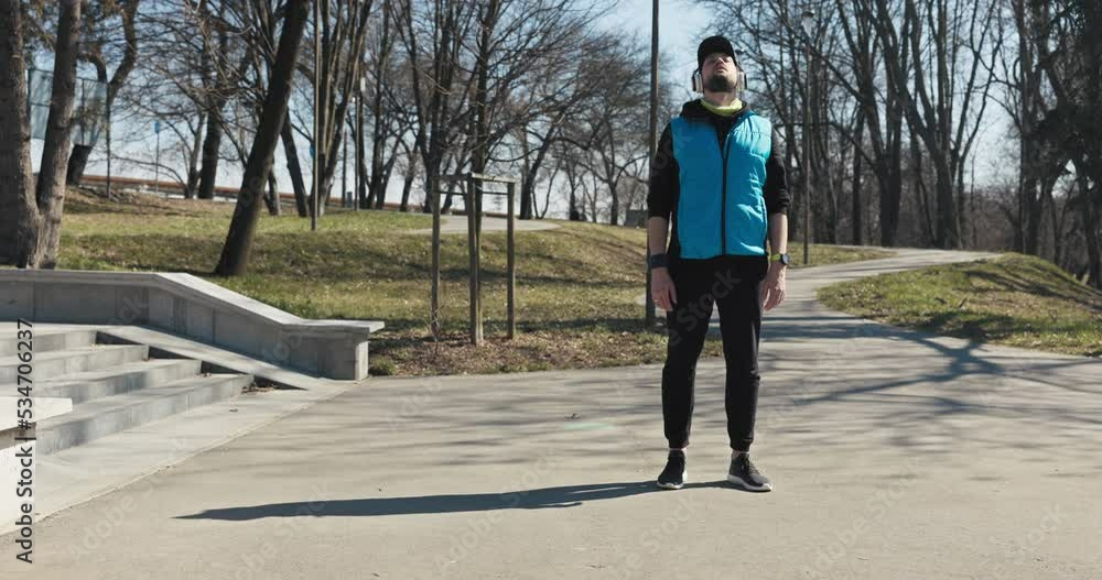 Young tall man came to the park and does warm-up before running ...