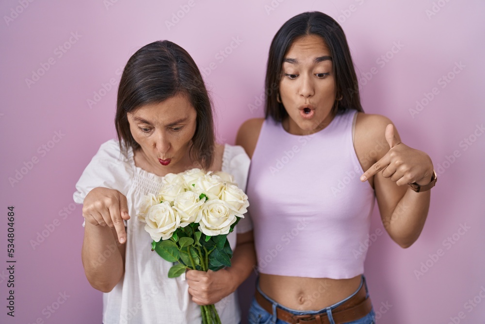 Hispanic mother and daughter holding bouquet of white flowers pointing ...