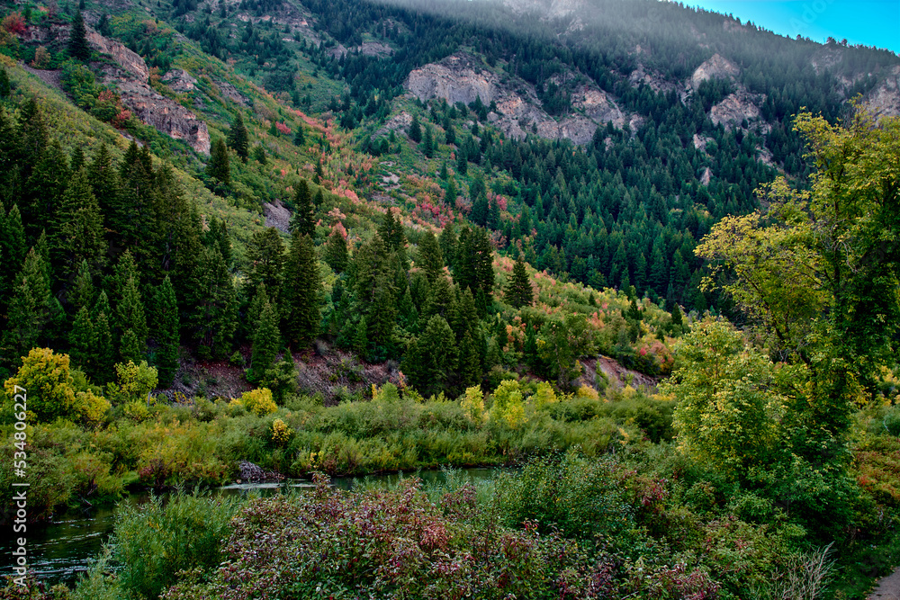 Morning sunlight peeks over a mountain ridge as the Provo river flows ...