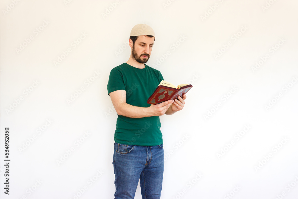 Young bearded muslim man wearing a taqiyah (cap) and reading a Quran ...