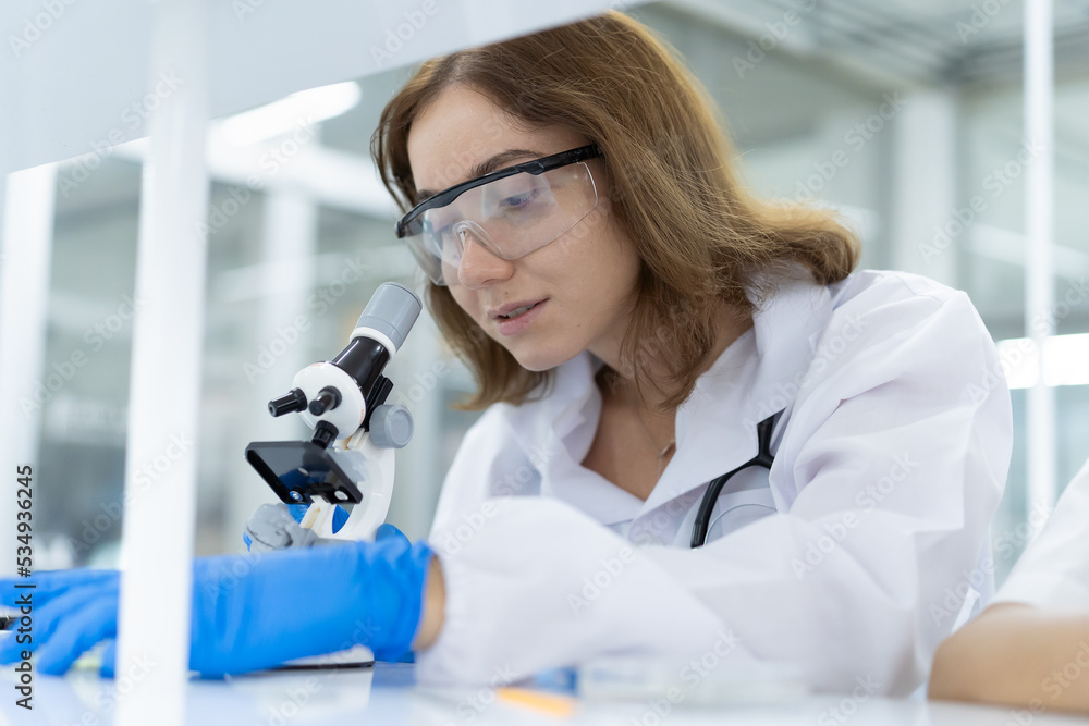 Woman doctor looking through microscope doing analysis for germs and ...