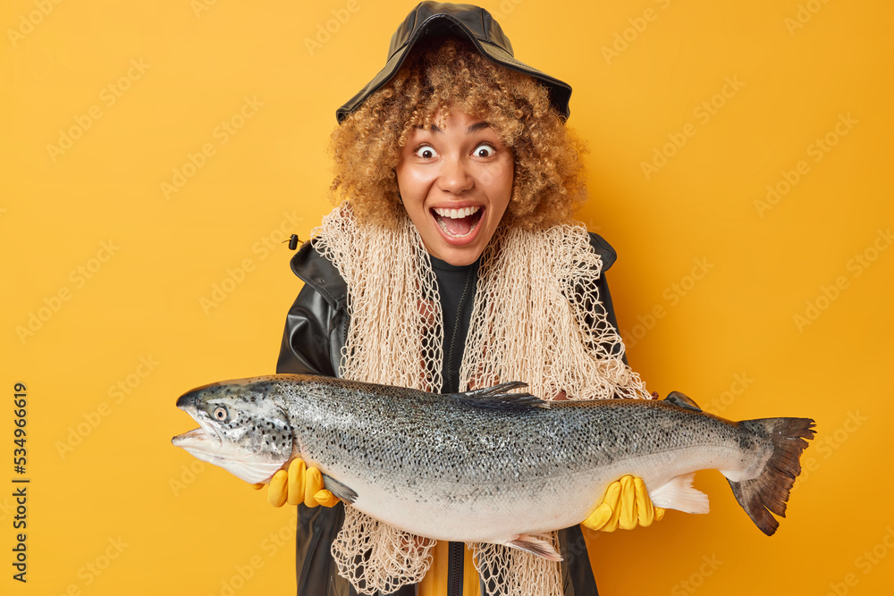 Indoor shot of surprised cheerful curly woman caught very big fish ...