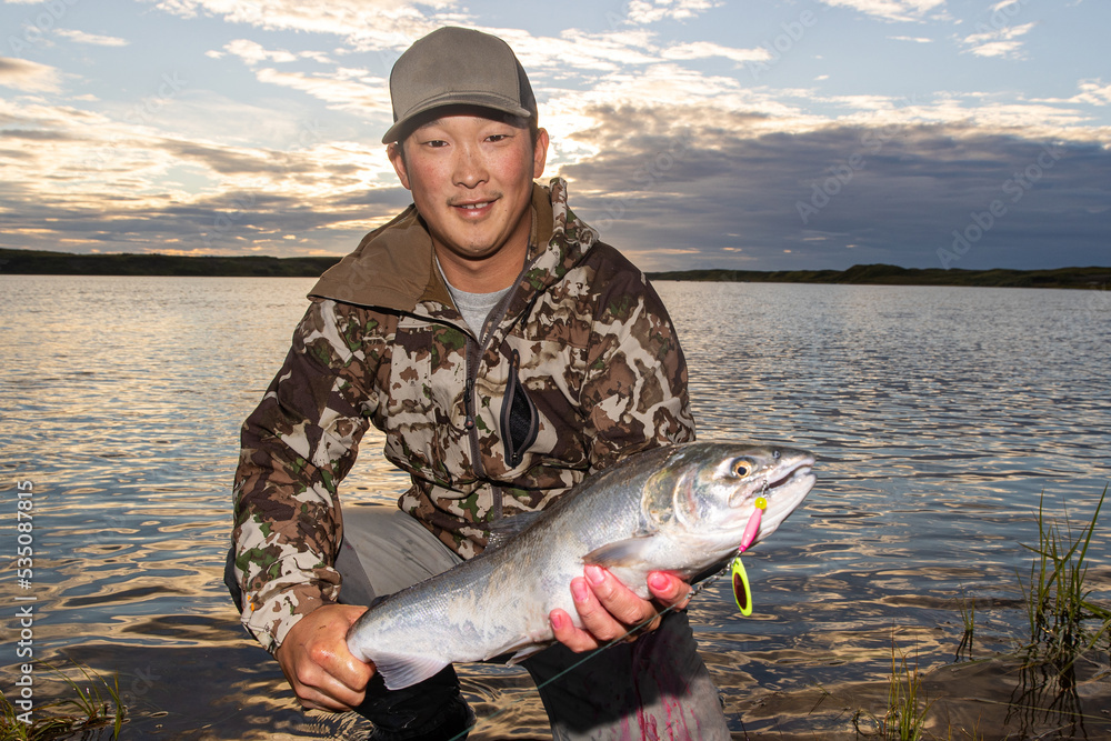 Happy fisherman holding fresh caught silver coho salmon on the bank of ...