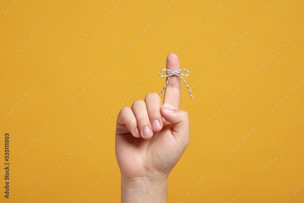 Man showing index finger with tied bow as reminder on orange background ...