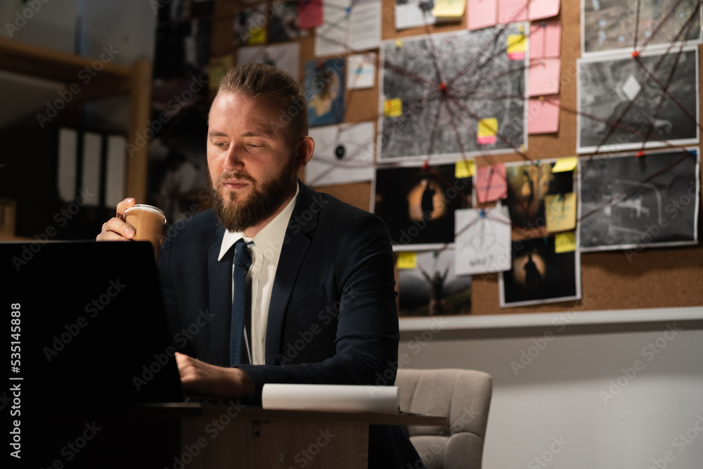 Detective working in office using computer at night, drinking coffee at ...
