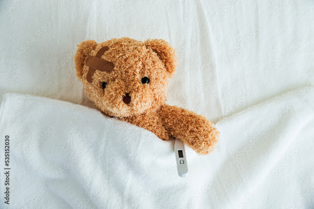 Teddy bear in bed with thermometer and bandage Stock Photo | Adobe Stock