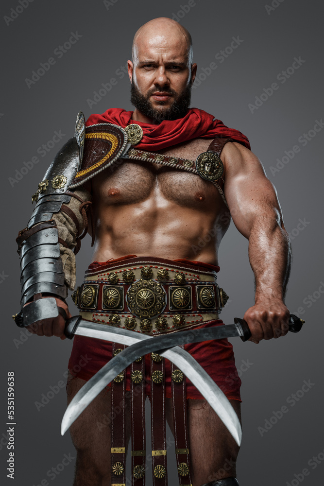 Portrait of ancient gladiator with bare torso posing with dual swords ...