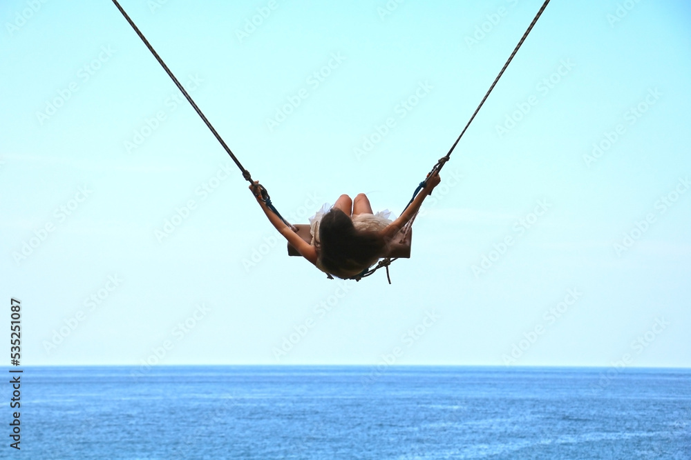 Young woman on a swing high in the sky against a background of ocean ...