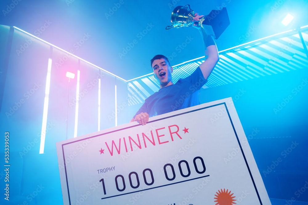 Winner gamer young man holding cup trophy and check prize of victors ...