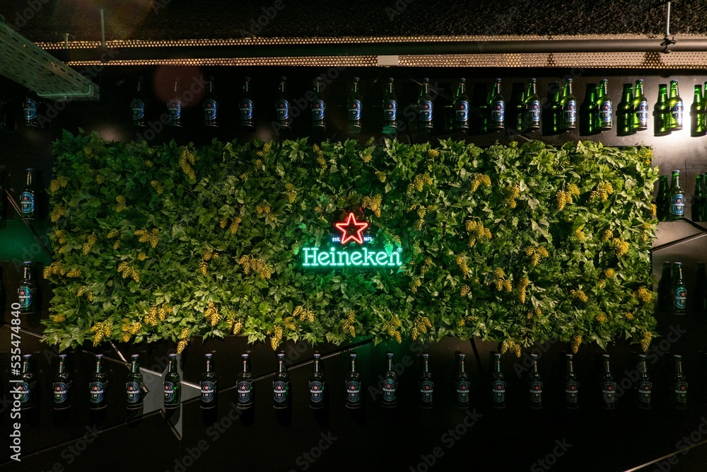 Heineken logo with neon lights on the Hops bushes with empty bottles ...