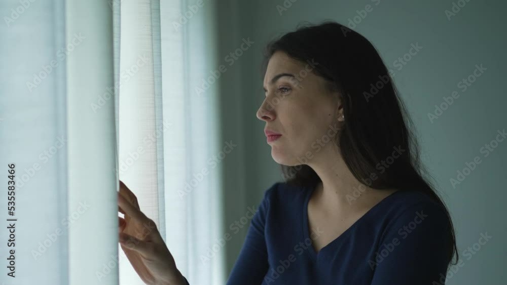 Anxious Woman standing by window peeking out in suspicion feeling ...
