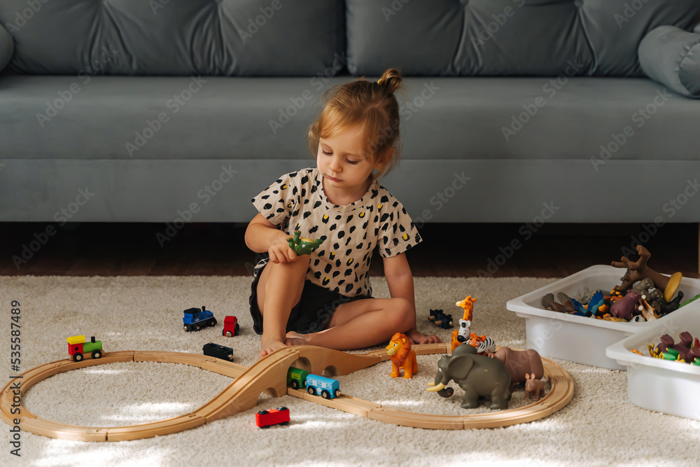 Kid girl builds a toy town and wooden railway. A little girl sitting on ...