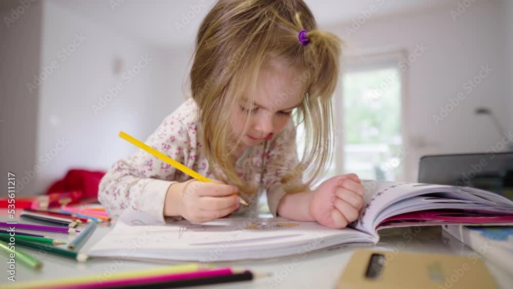 The kid is drawing at home. Little blonde girl is diligently coloring ...