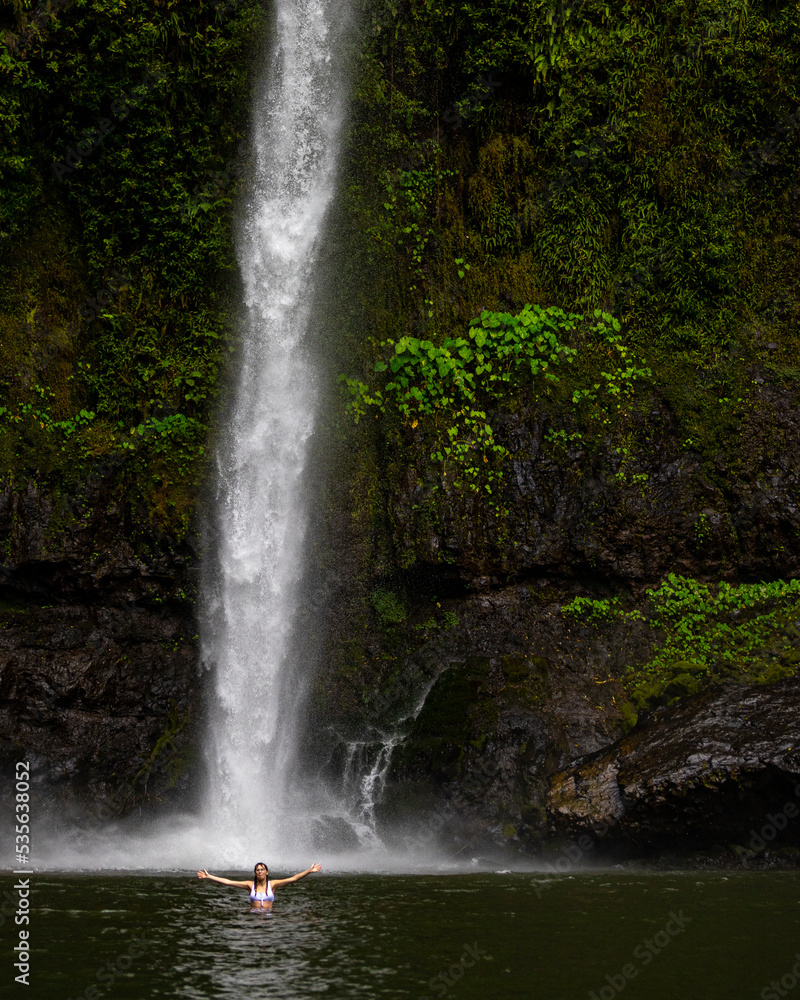 beautiful woman takes a bath in a powerful tropical waterfall ...