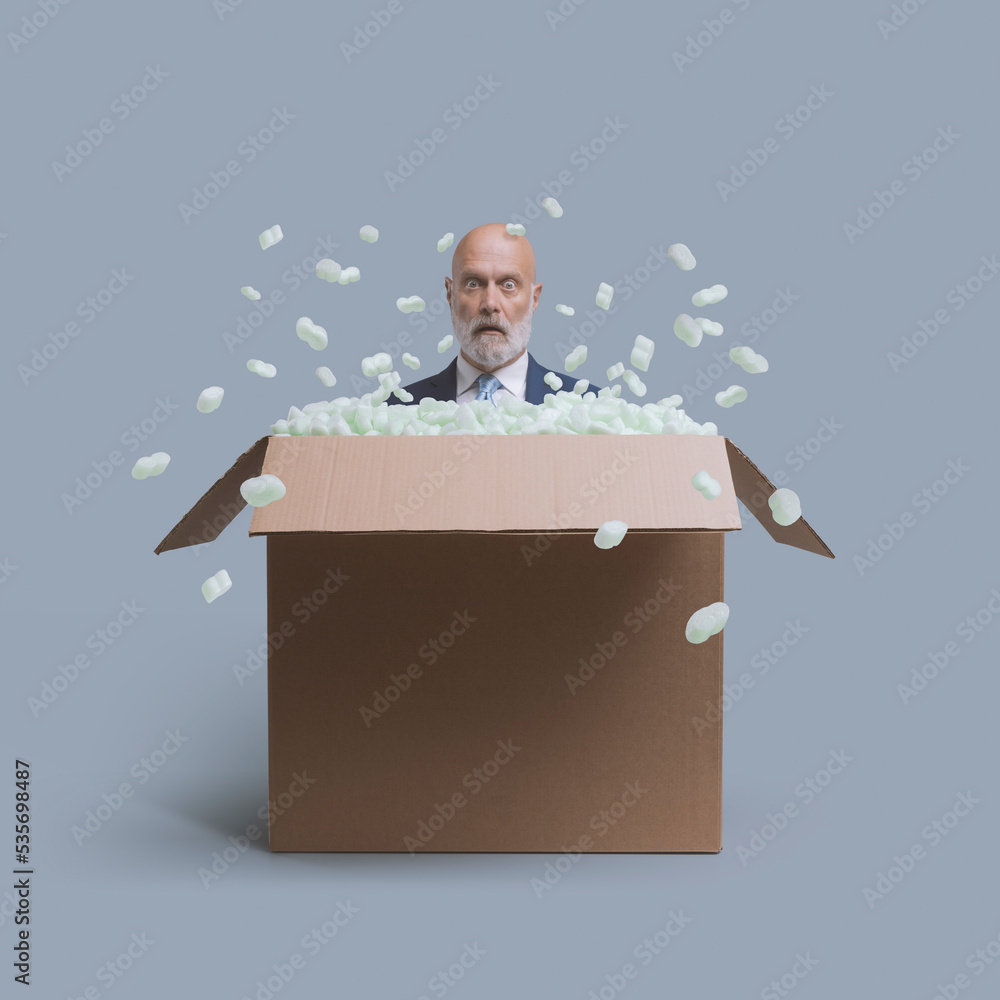 Surprised businessman coming out from a box Photos | Adobe Stock