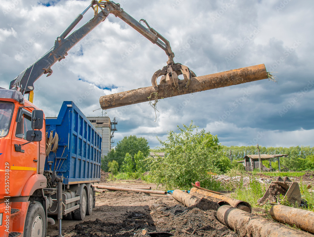 Special loader with help of grab grabbed old cast-iron pipe and loads ...