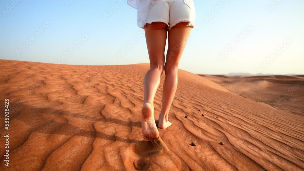 Close-up beautiful female legs in shorts walking on desert sand ...