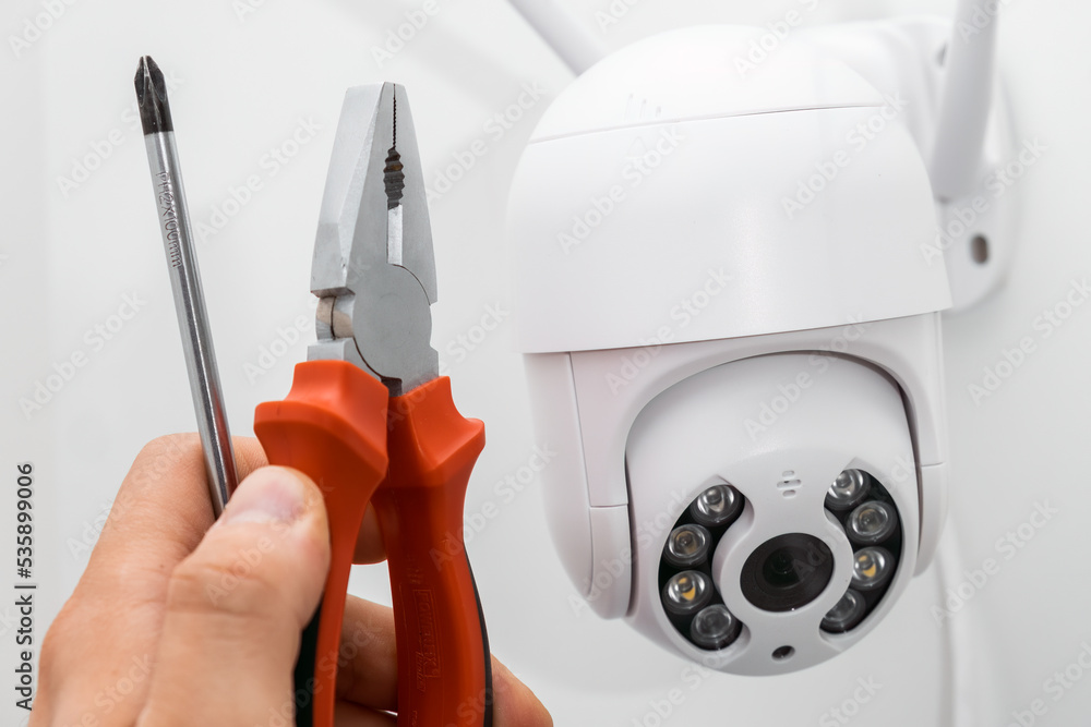 Technician installing CCTV camera using pliers and screwdriver outside ...