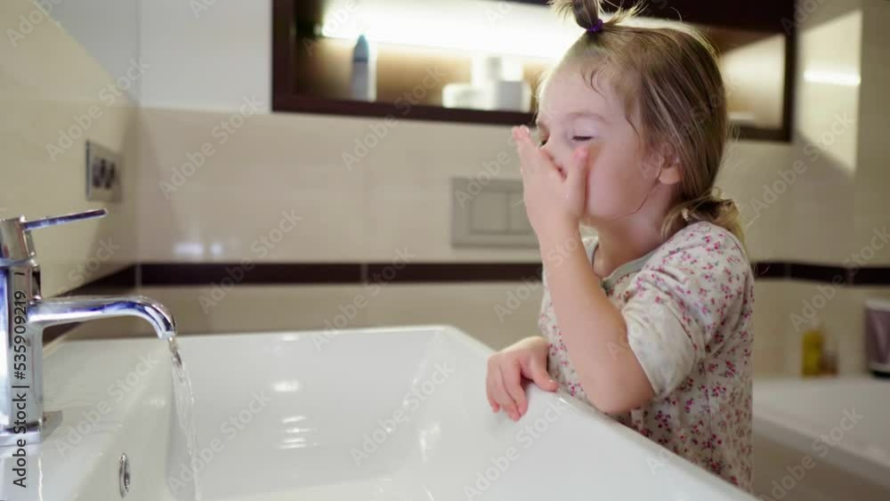 Little girl washes her face with cool water in the bathroom. Children's ...