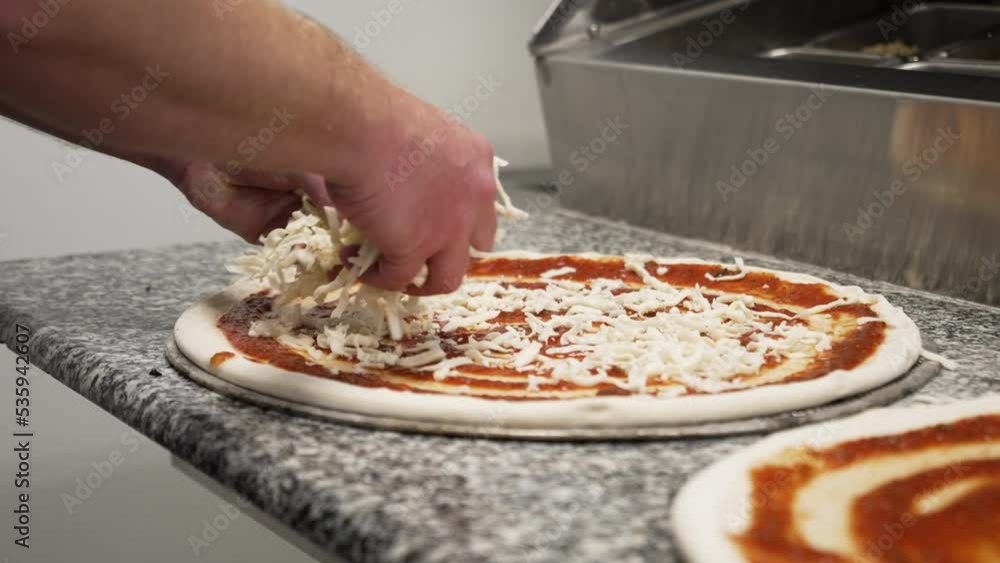 Chef sprinkles handfuls of shredded mozzarella cheese over pizza dough ...
