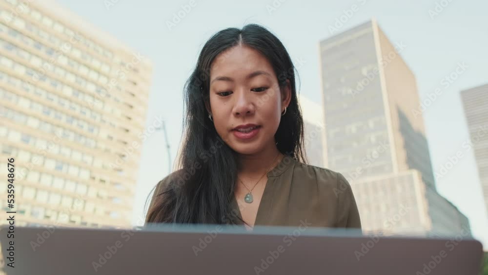 Close up, young girl uses laptop pc outside on modern buildings ...