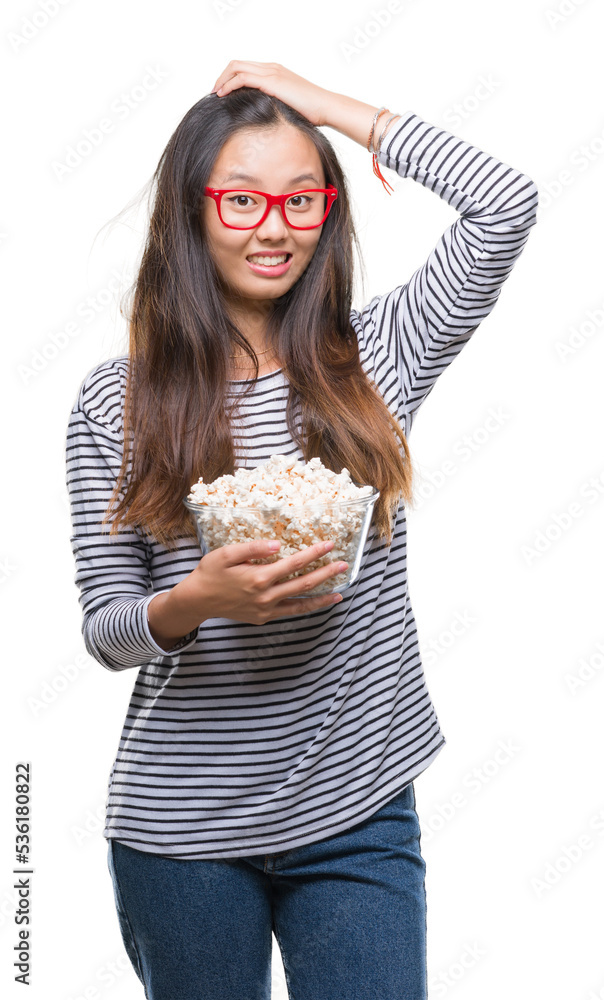 Young asian woman eating popcorn over isolated background stressed with ...