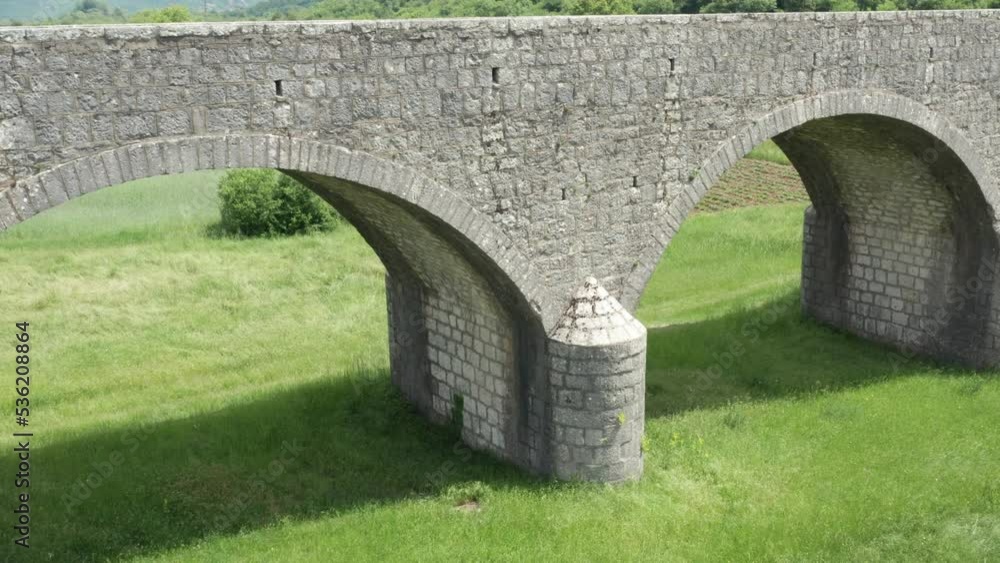 Vidéo Stock Old arch bridge made of stone over a green grassy field ...