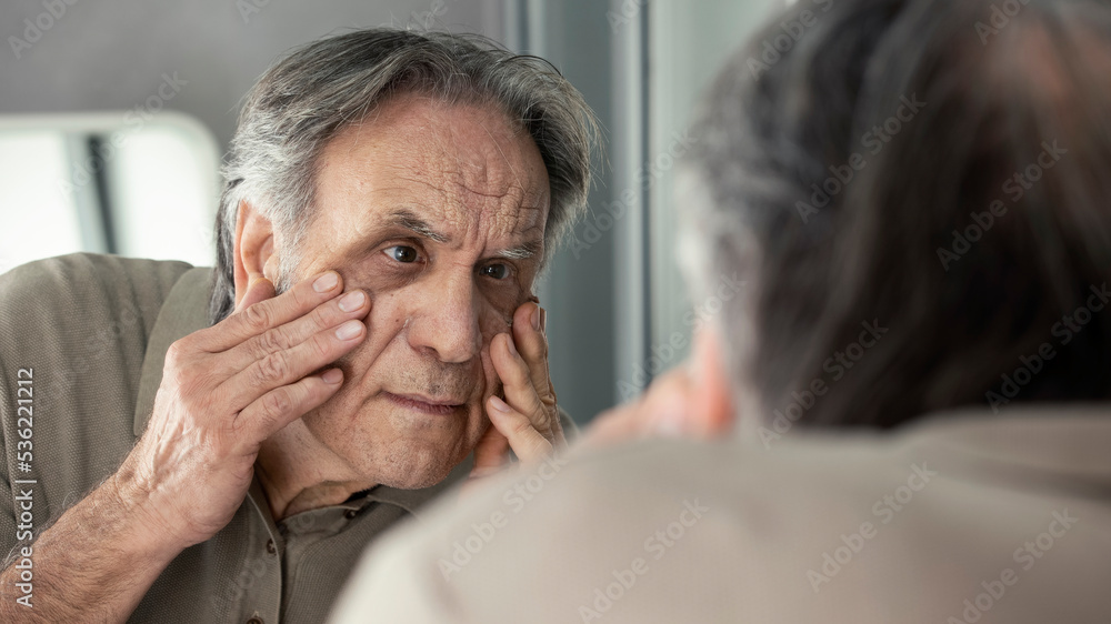 Old man examines his own eye and wrinkled in the mirror foto de Stock ...