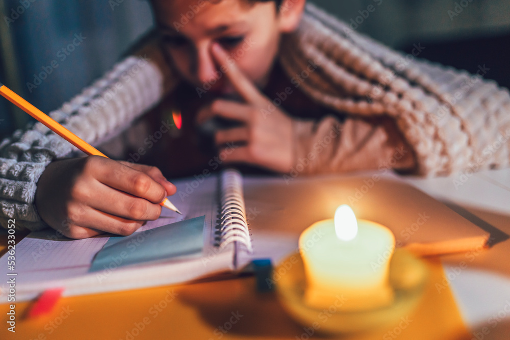 Little boy studying in low light with a burning candle. Power outage ...