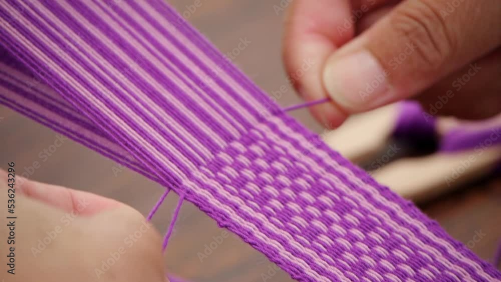 Fingers stringing and pressing purple and white yarn to create patterns ...