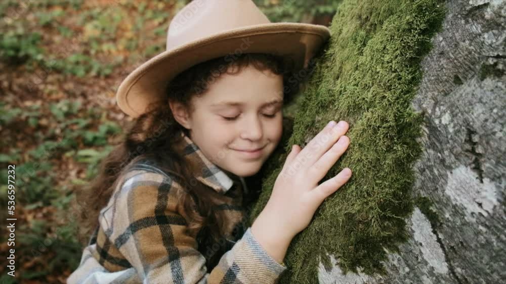 Happy cute little girl child in hat girl touch softly old tree bark ...