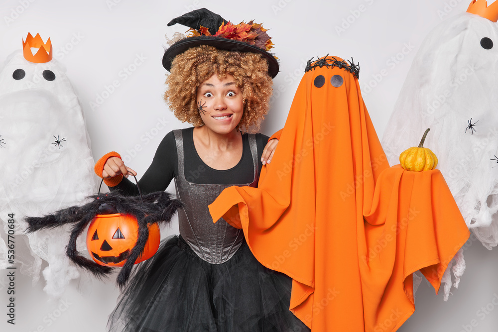 Curly haired female witch bites lips stares impressed at camera holds ...