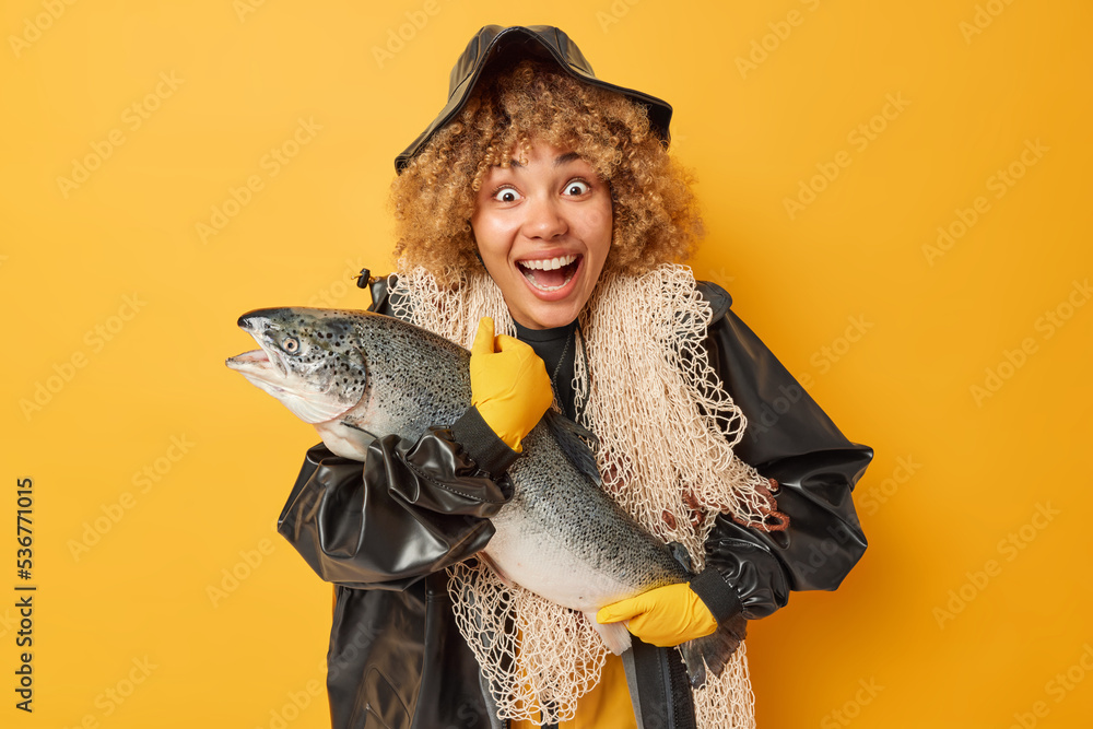 Positive curly haired successful excited fisherwoman carries big caught ...