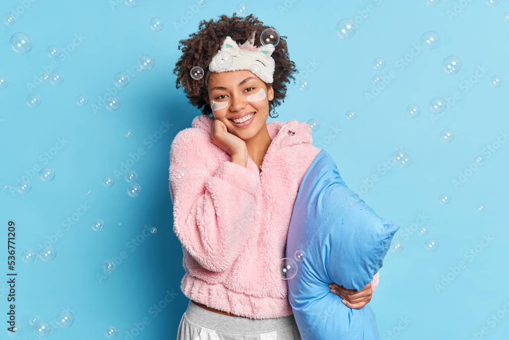 Horizontal shot of good looking curly haired woman dressed in pajama ...