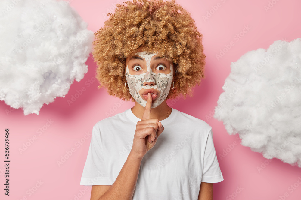 Shocked surprised woman with curly hair applies facial clay mask to ...