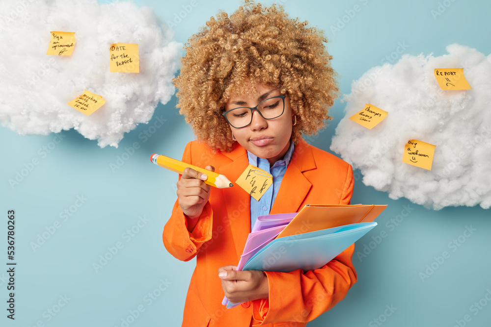 Serious female student looks attentibely at folders with papers holds ...