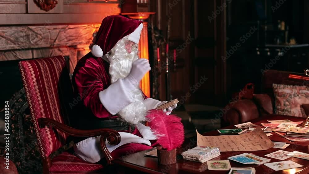 Santa Claus writing the Christmas cards sitting near the fireplace ...
