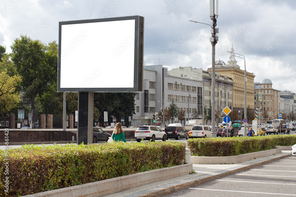 Billboard in the city by a green hedge and a busy street during the day ...