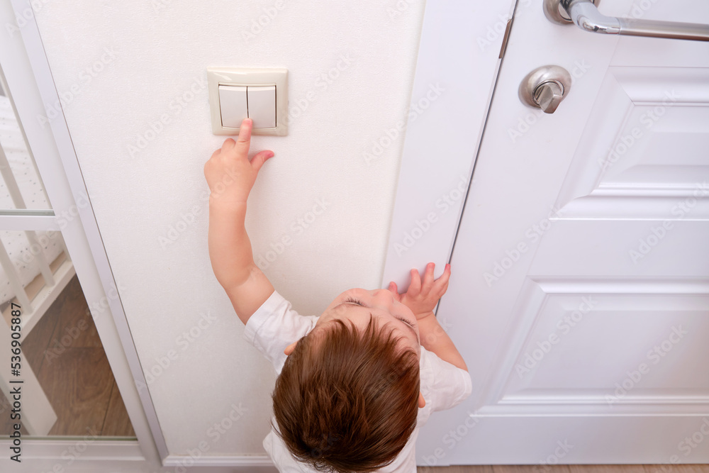 Toddler baby reaches for the light switch, child hand turns on the lamp ...