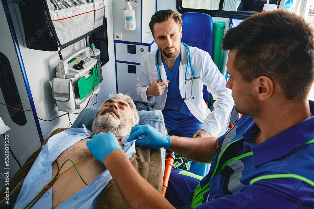 Cardiac patient in ambulance. Paramedics performing ECG on male vicitm ...