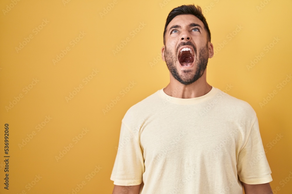 Handsome hispanic man standing over yellow background angry and mad ...
