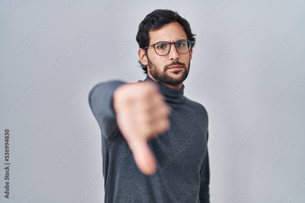 Handsome latin man standing over isolated background looking unhappy ...