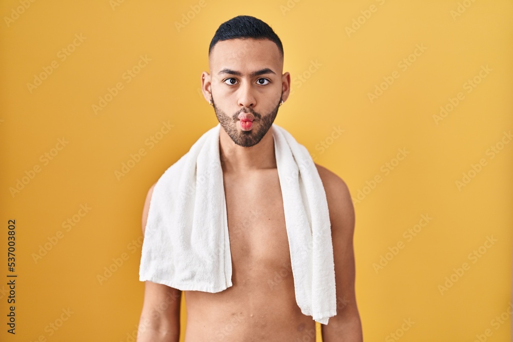 Young hispanic man standing shirtless with towel making fish face with ...
