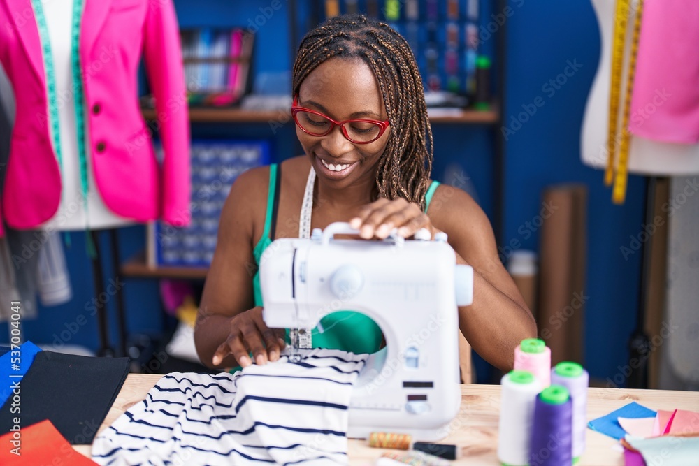 African american woman tailor smiling confident using sewing machine at ...