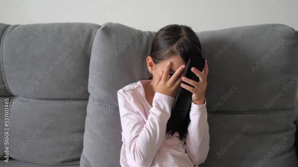 Portrait scared little kid while watching TV. Young Girl sit on sofa ...