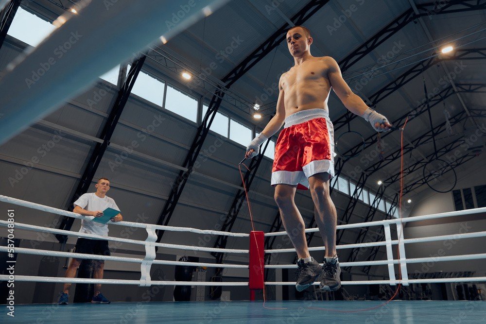 Jumping rope. Young sportive man, boxer workout at boxing ring at ...