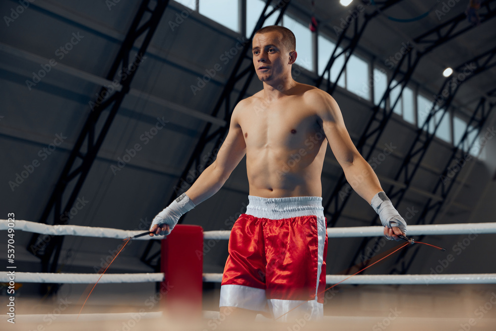 Jumping rope. Young sportive man, boxer workout at boxing ring at ...