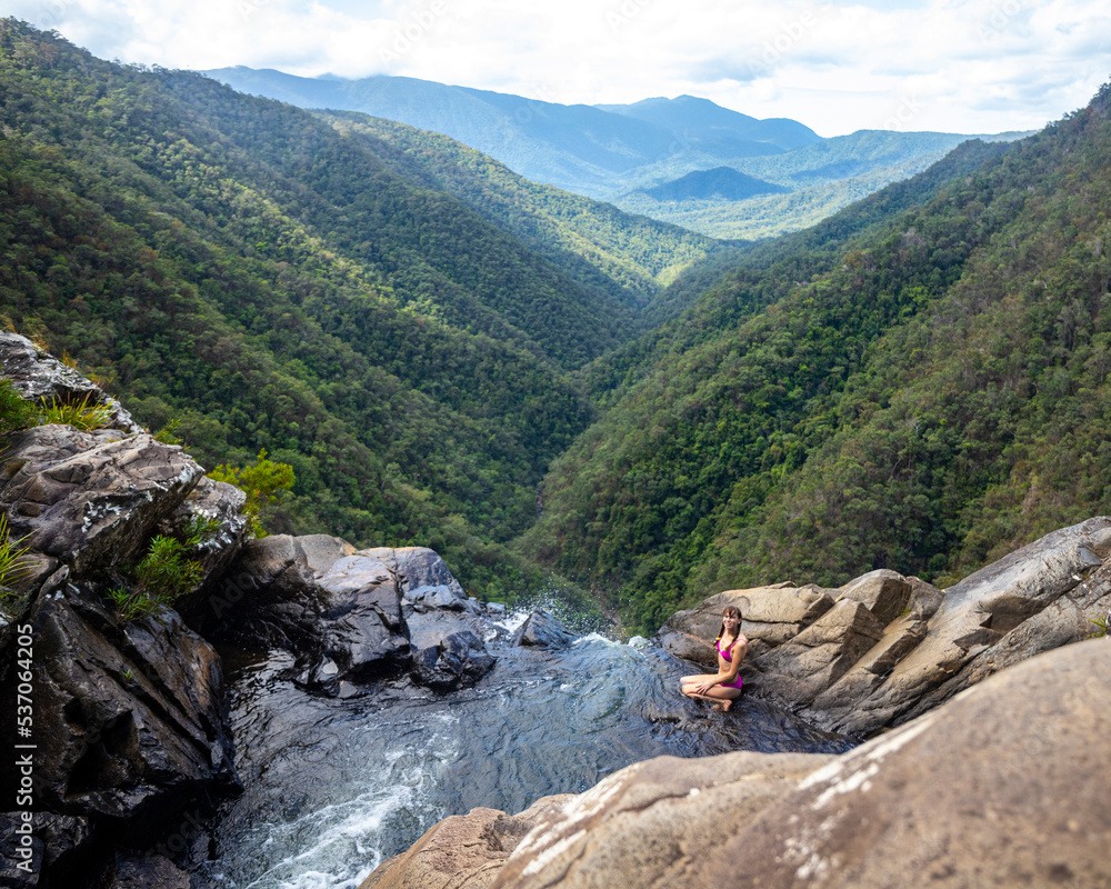 beautiful girl in bikini sits over precipice at top of windin falls ...