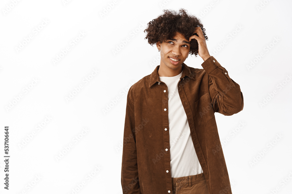 Confused gen-z guy scratch his curly hair and looks puzzled, clueless ...
